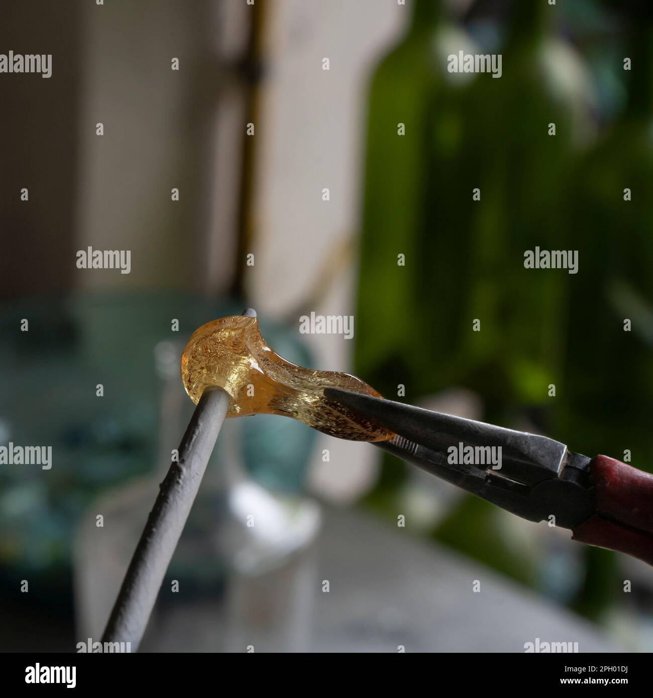 Pulling and stretching a hot lump of yellow glass with long nose pliers ...