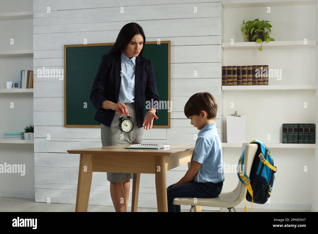 Teacher with alarm clock scolding pupil for being late in classroom ...