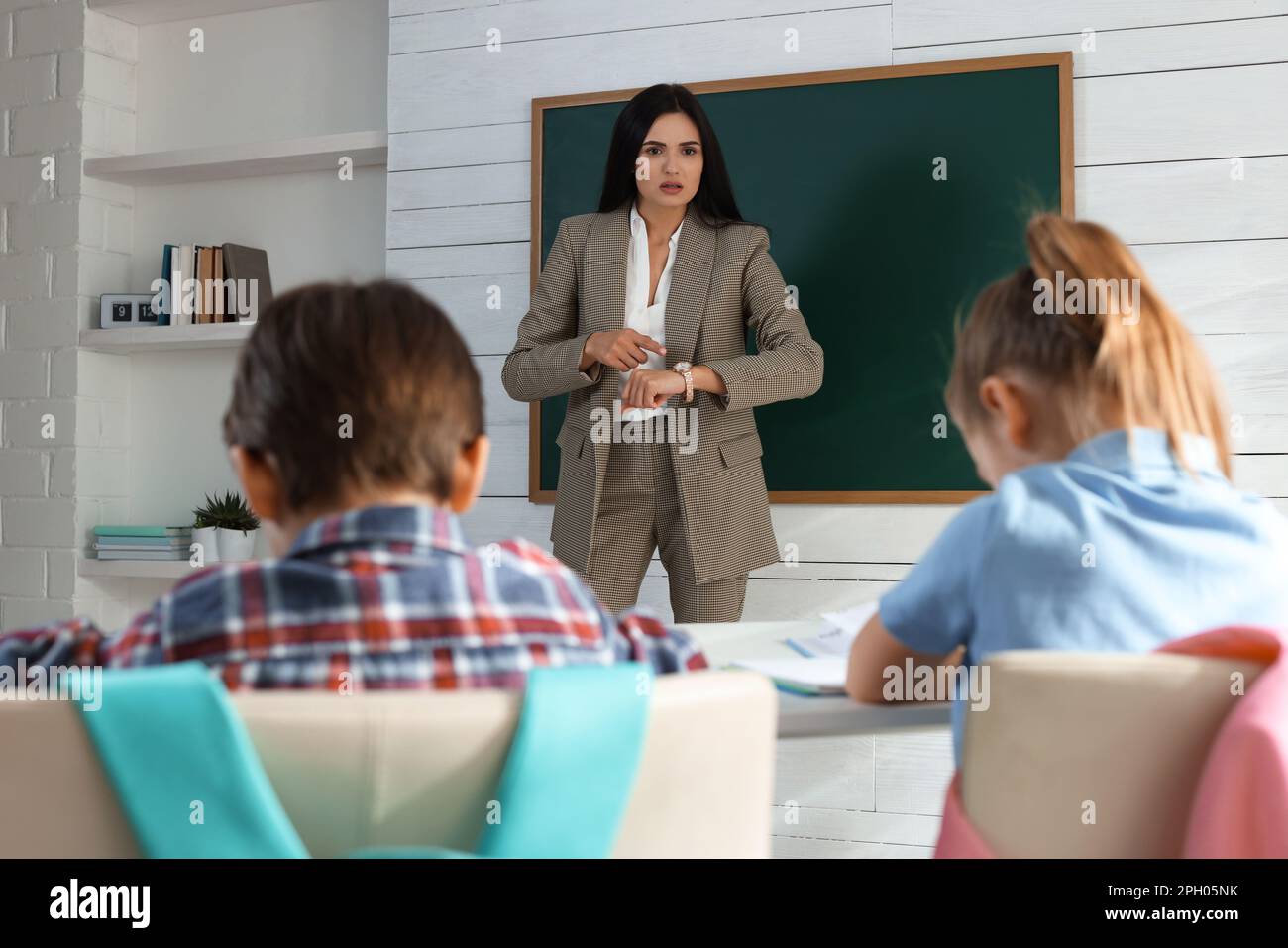 Teacher pointing on wrist watch while scolding pupils for being late in ...