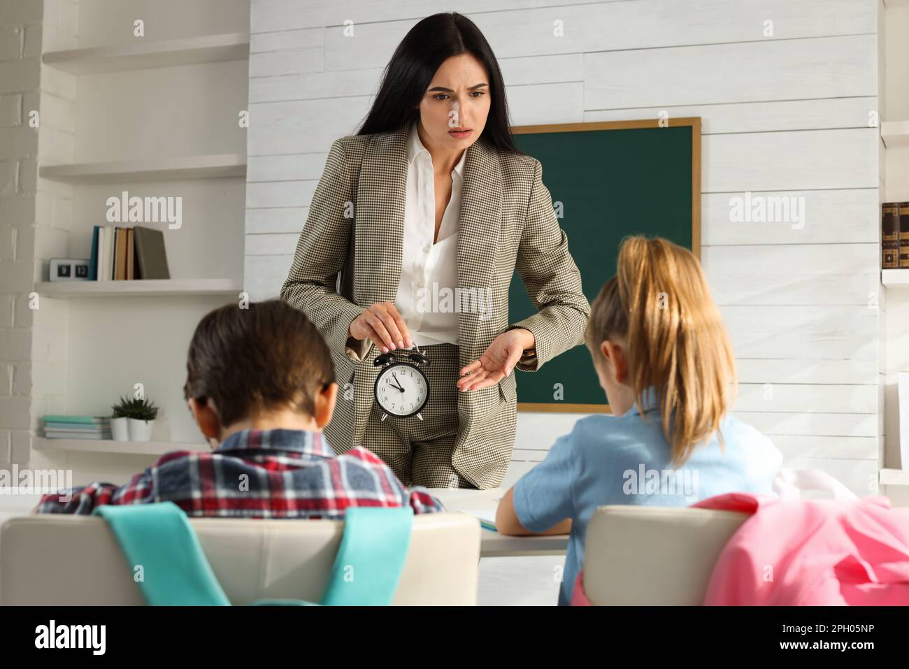 Teacher with alarm clock scolding pupils for being late in classroom ...