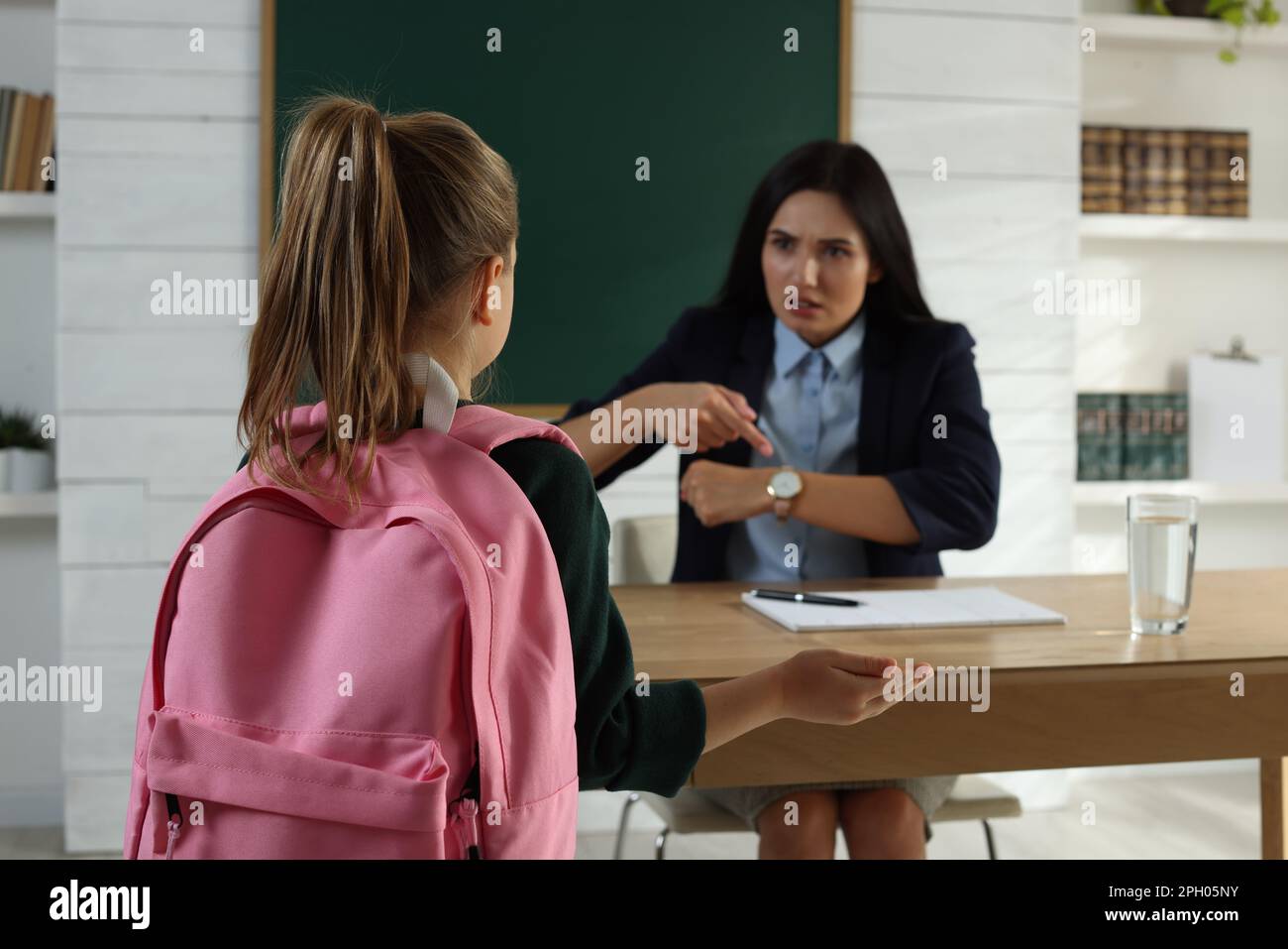 Teacher pointing on wrist watch while scolding pupil for being late in ...