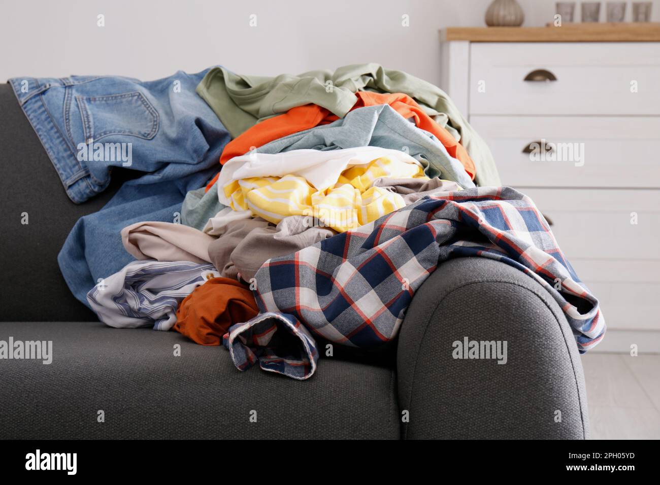 Messy pile of dirty clothes on sofa in living room. Tidying up method ...