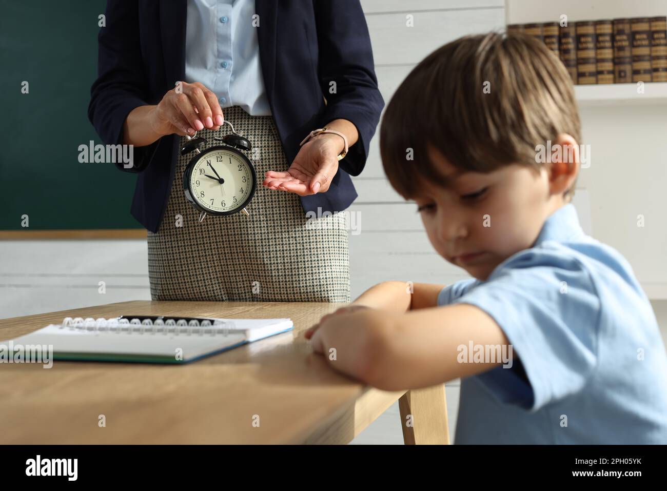 Teacher scolding pupil for being late in classroom, focus on alarm ...