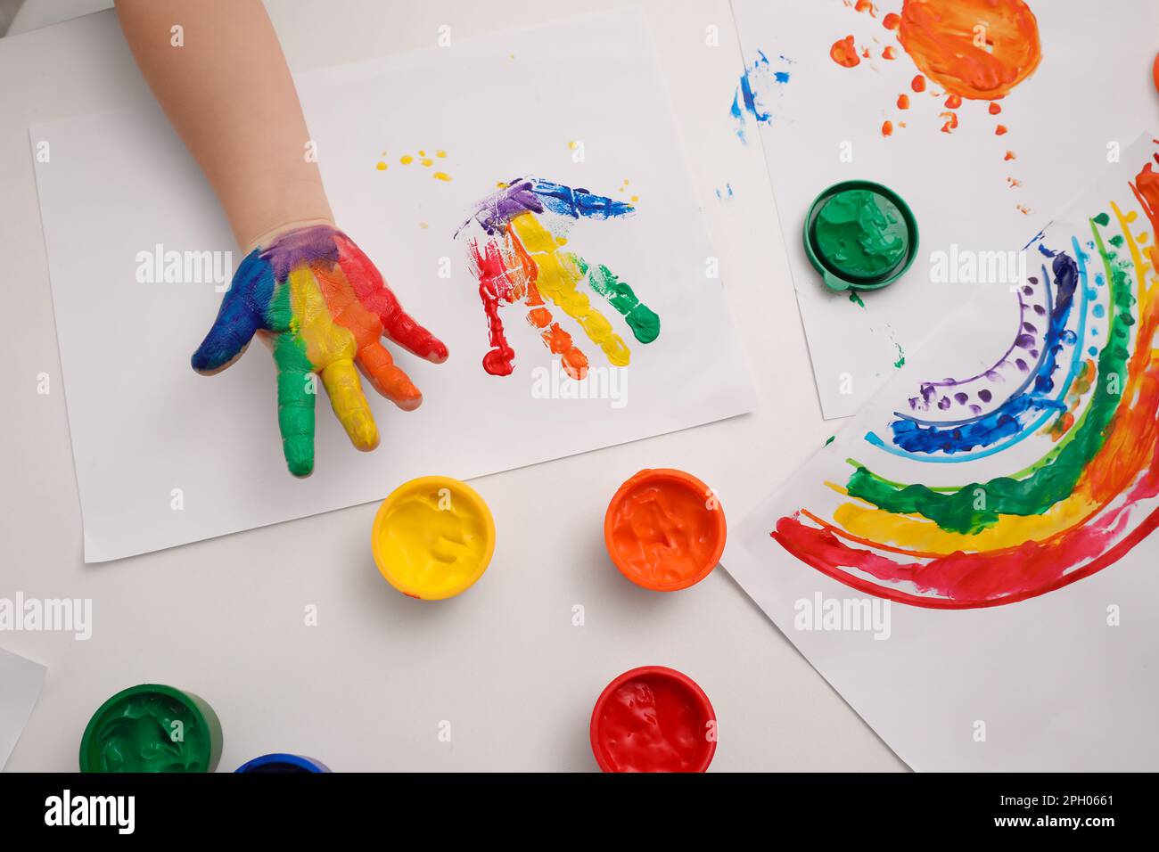 Little child making hand print on paper with painted palm at white ...