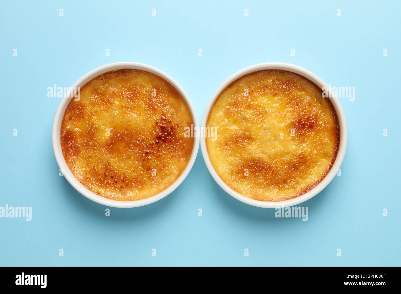 Delicious creme brulee in ramekins on light blue background, flat lay ...