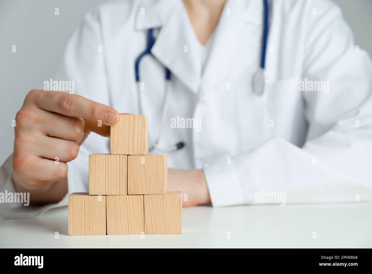 Doctor building pyramid of blank wooden cubes on white table against ...