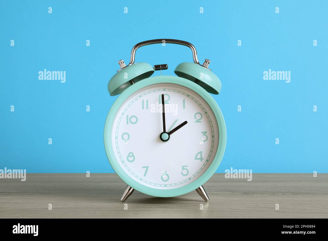 Turquoise alarm clock on wooden table against light blue background ...