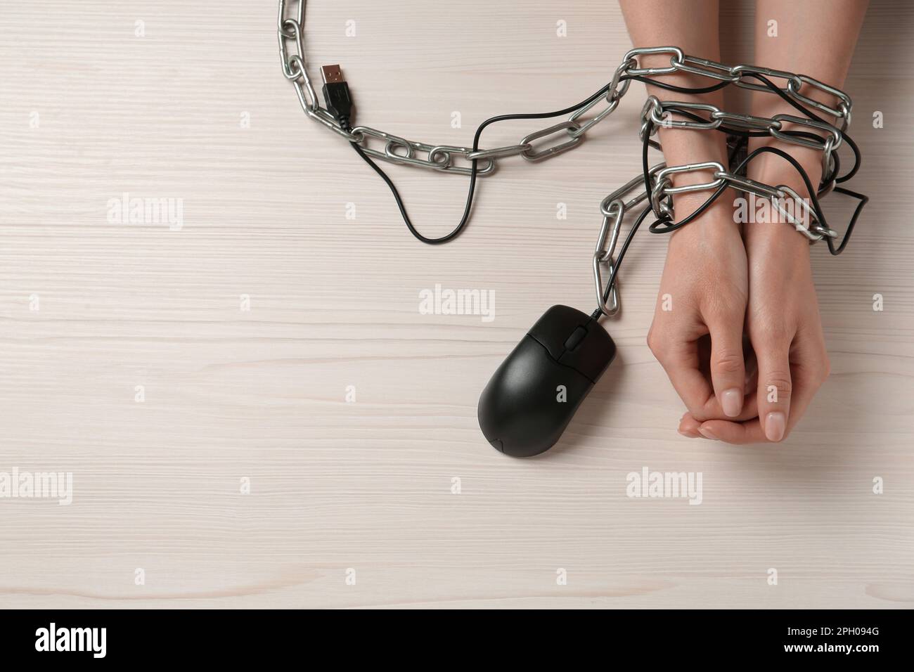 Woman showing hands chained with computer mouse cable at white wooden ...