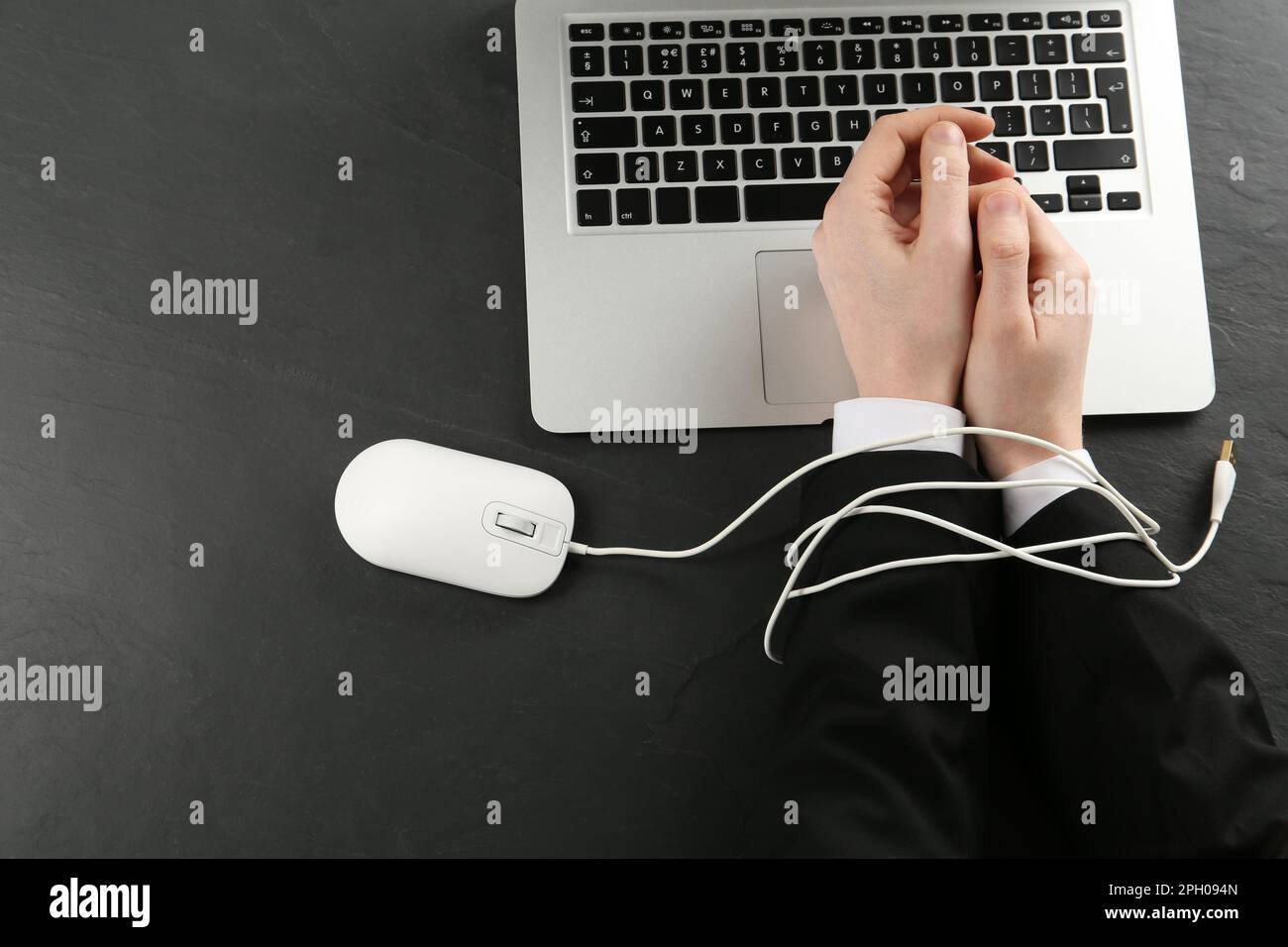 Man showing hands tied with computer mouse cable near laptop at black ...