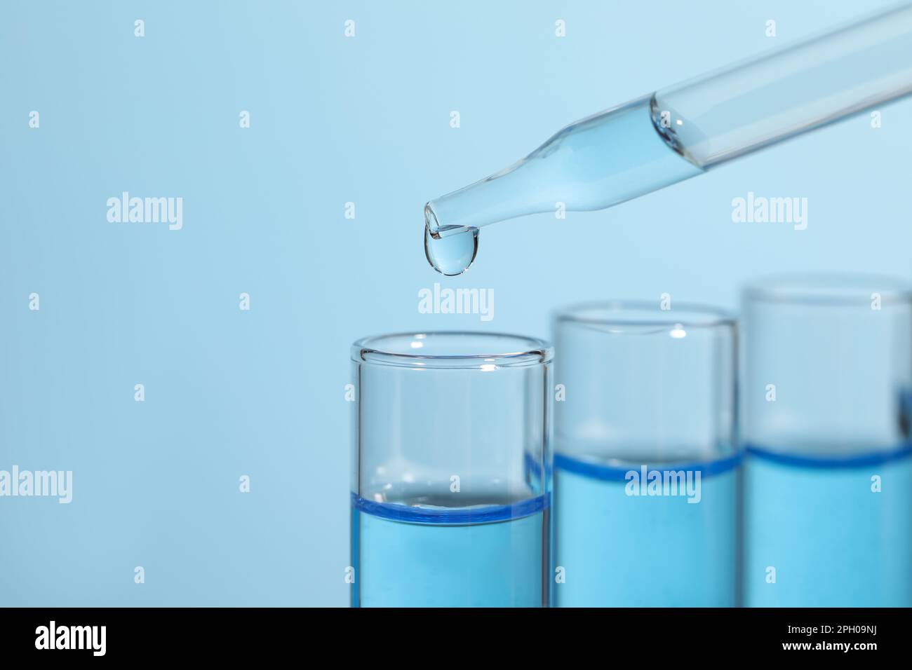 Dripping reagent into test tube on light blue background, closeup ...