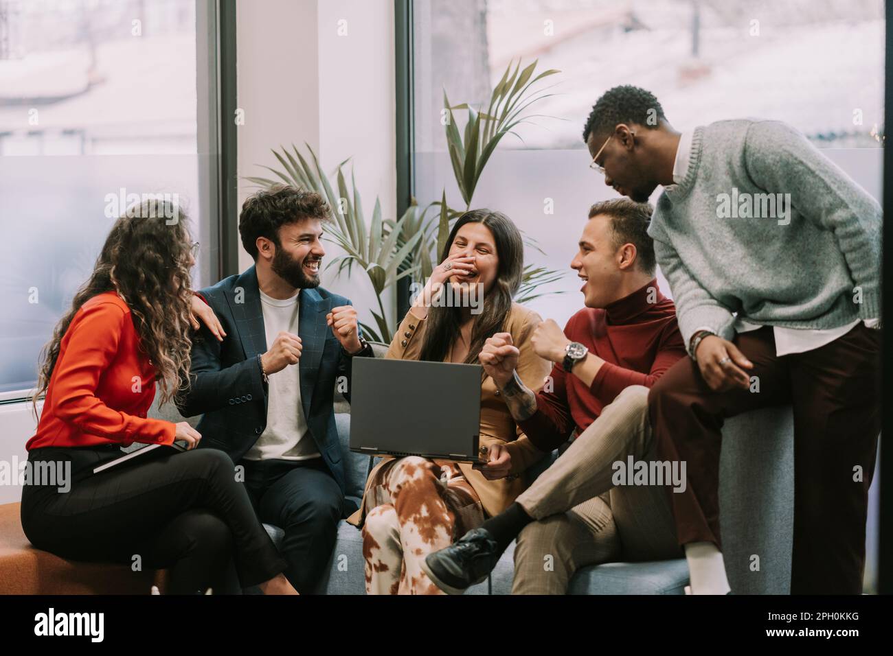 Five diverse coworkers sitting on gray sofa at the office, watching ...