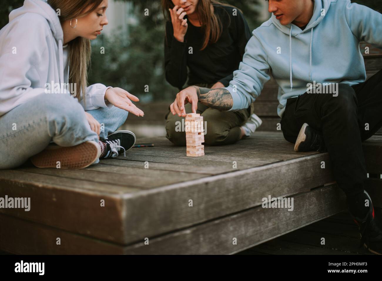 Three friends playing jenga at the park while sitting on the wooden ...