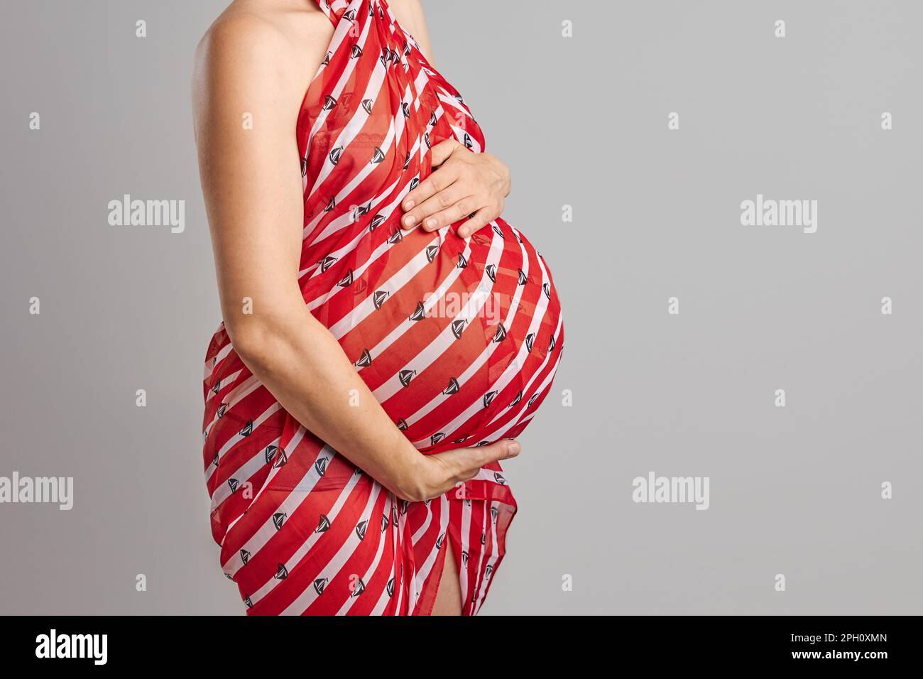 Pregnant woman touching her tummy standing over plain background ...