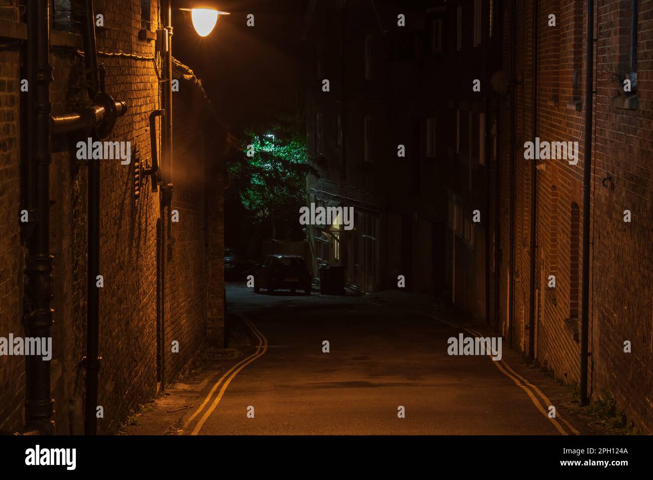 A single dim streetlight illuminates the view down the empty narrow ...