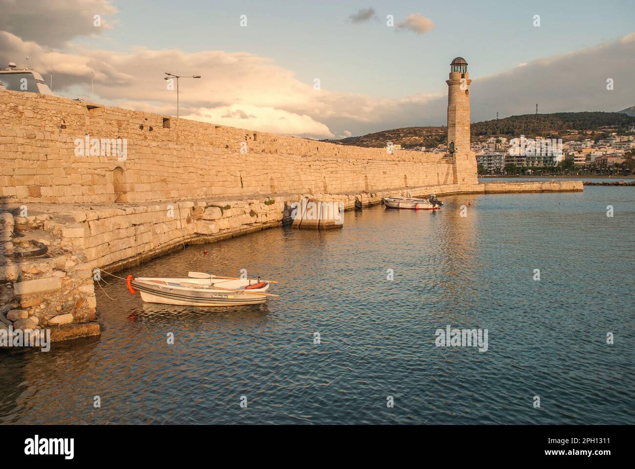 Evening sun warms the wall and lighthouse at the old Venetian harbour ...