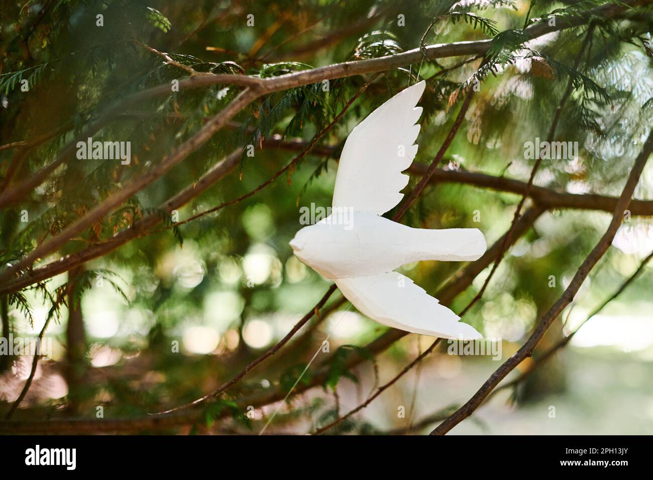 White bird decorative wooden figure suspended on tree branch in public ...