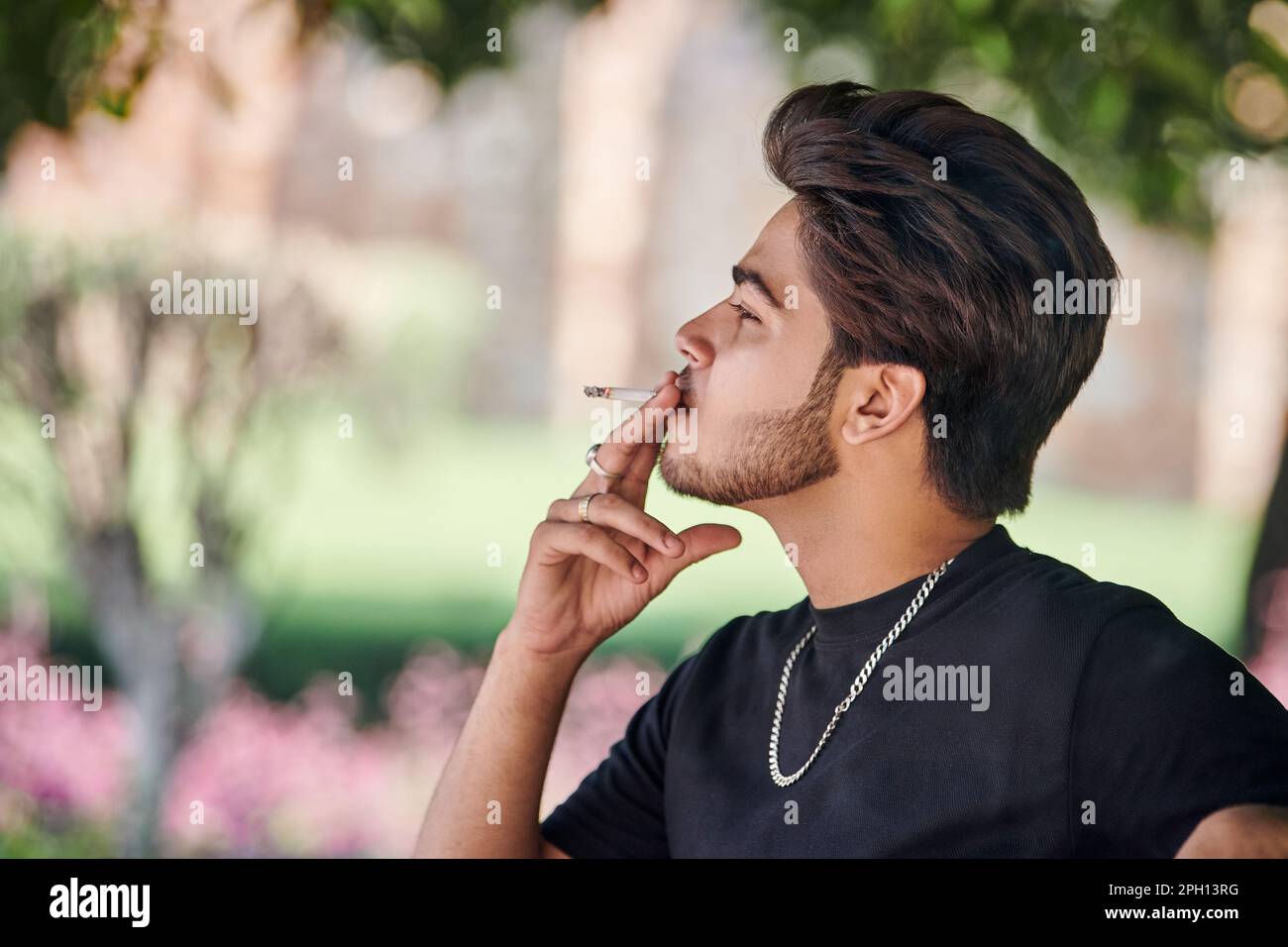 Young indian man smoker portrait in black t shirt and silver neck chain ...