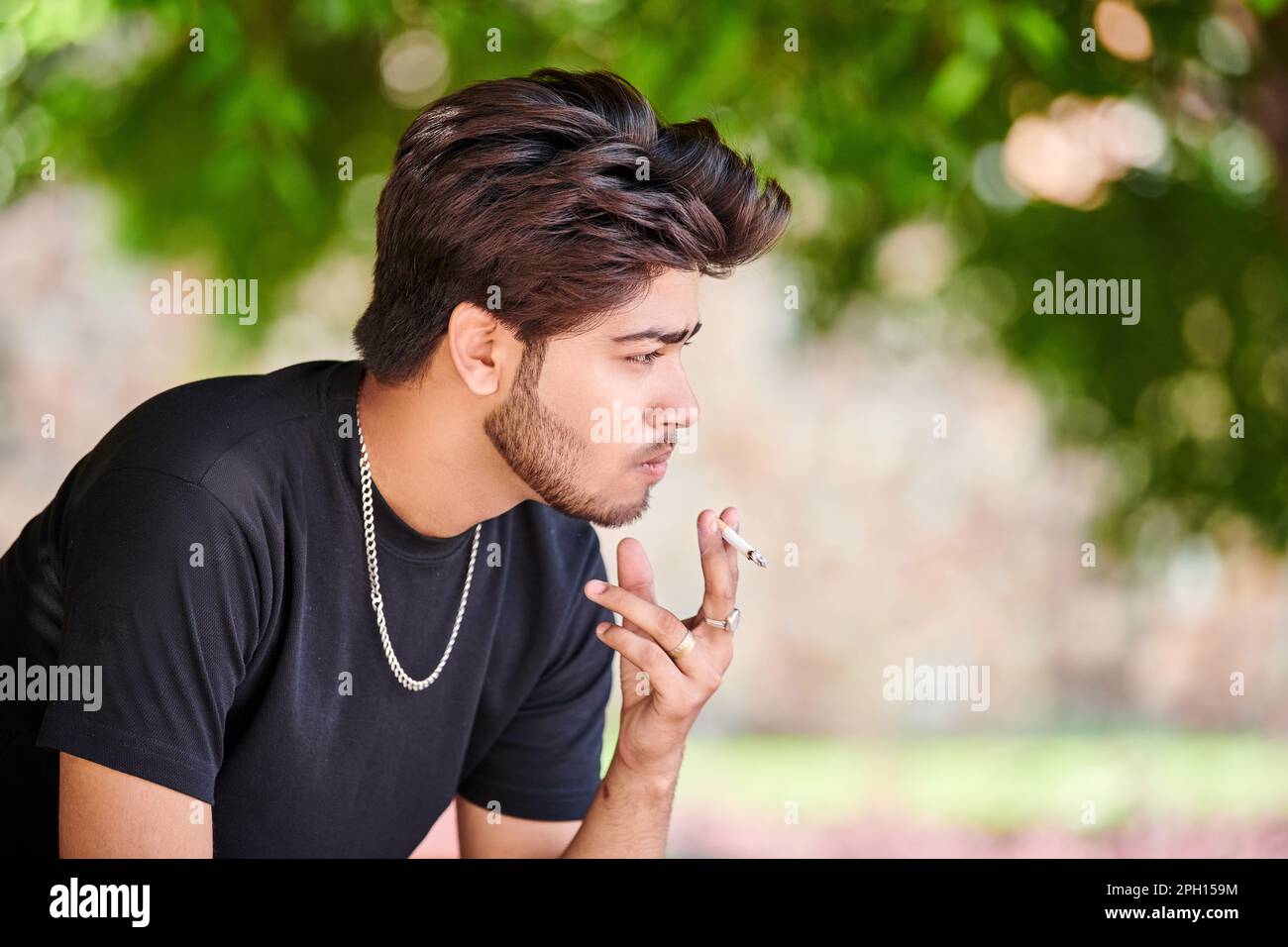 Young indian man smoker portrait in black t shirt and silver neck chain ...