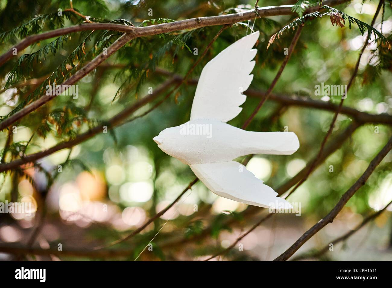 White bird decorative wooden figure suspended on tree branch in public ...