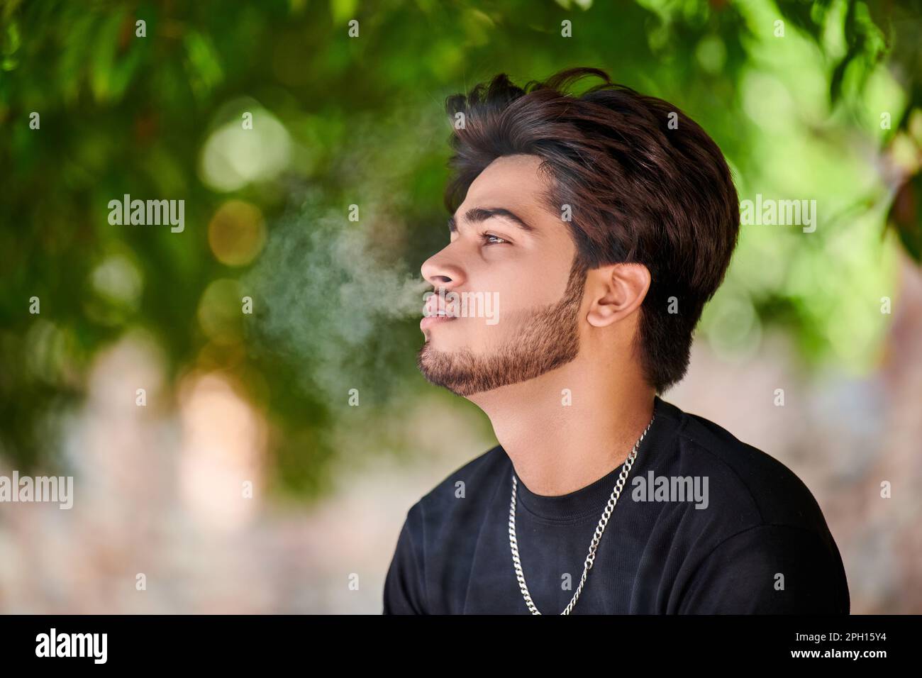 Attractive indian man smoker exhales cigarette smoke portrait in black ...