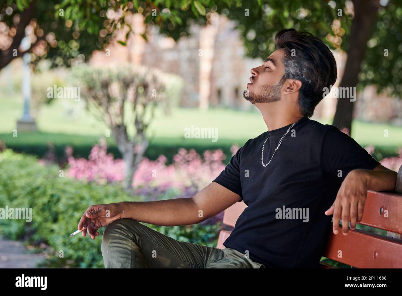 Attractive indian man smoker exhales cigarette smoke portrait in black ...