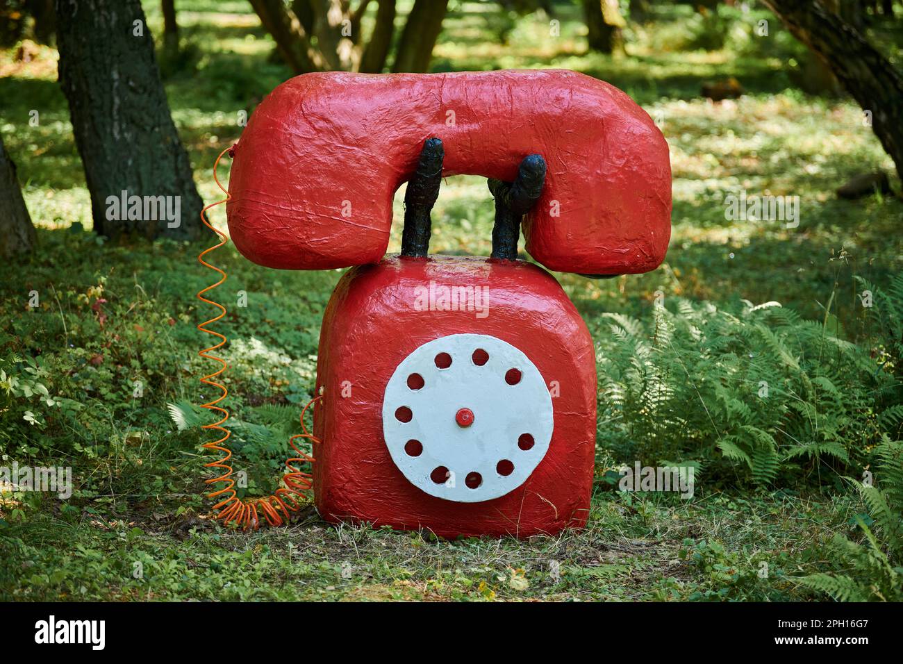 Statue of big retro red telephone with rotary dial art object on green ...