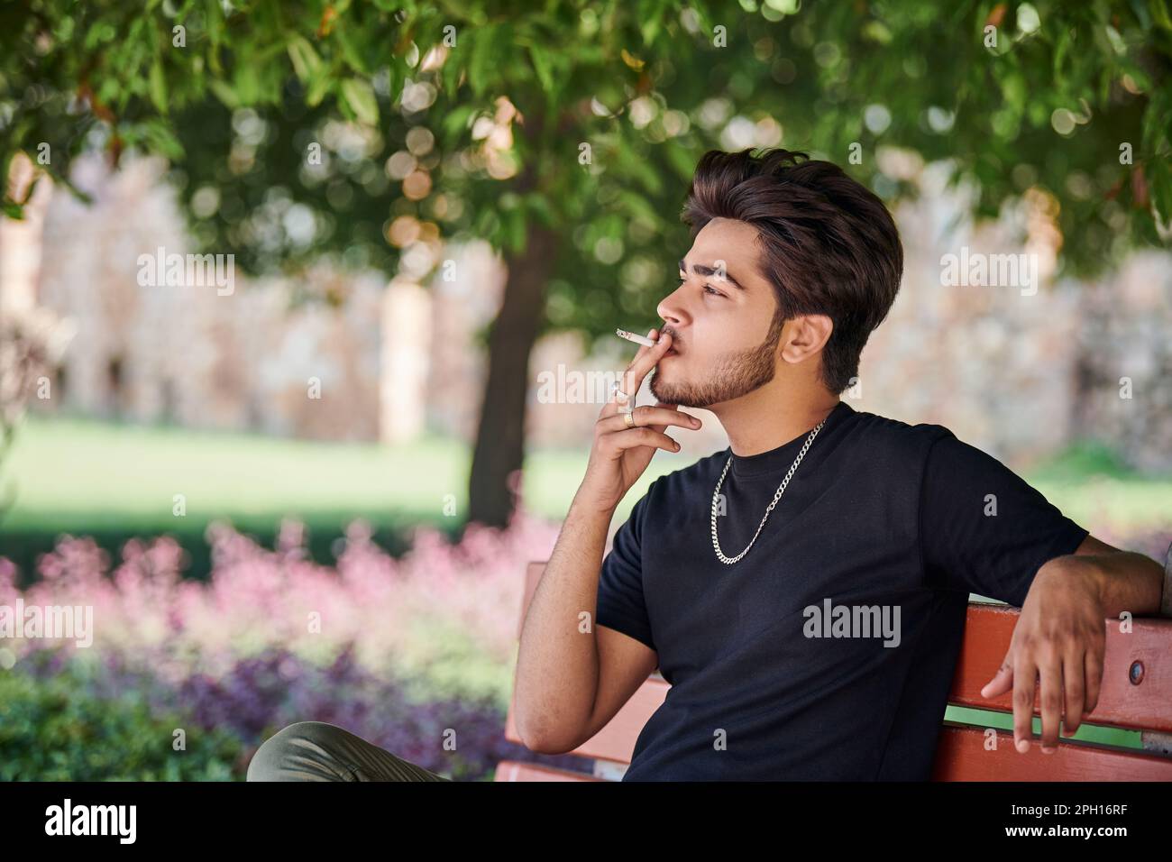 Young indian man smoker portrait in black t shirt and silver neck chain ...