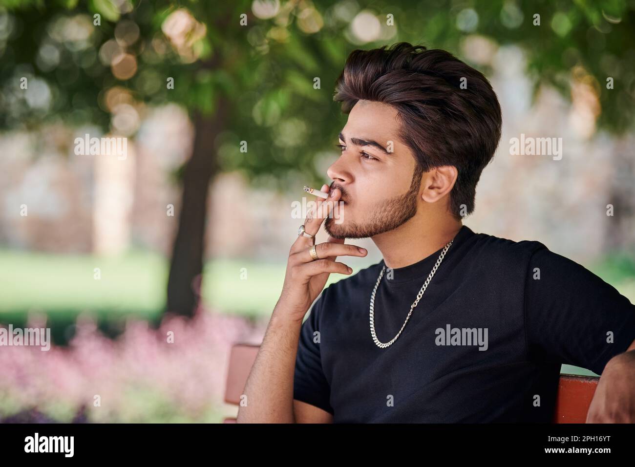 Young indian man smoker portrait in black t shirt and silver neck chain ...
