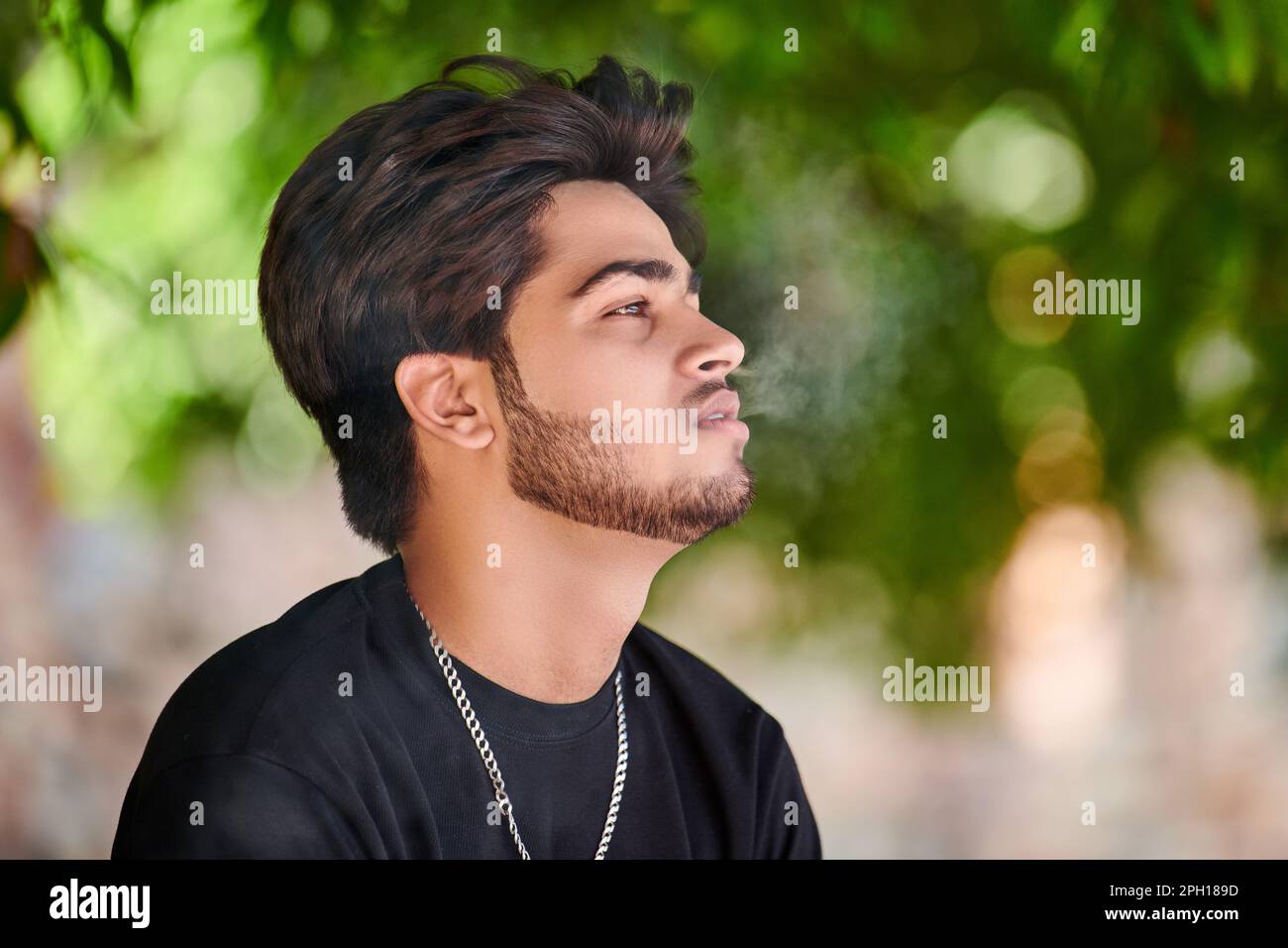 Attractive indian man smoker exhales cigarette smoke portrait in black ...