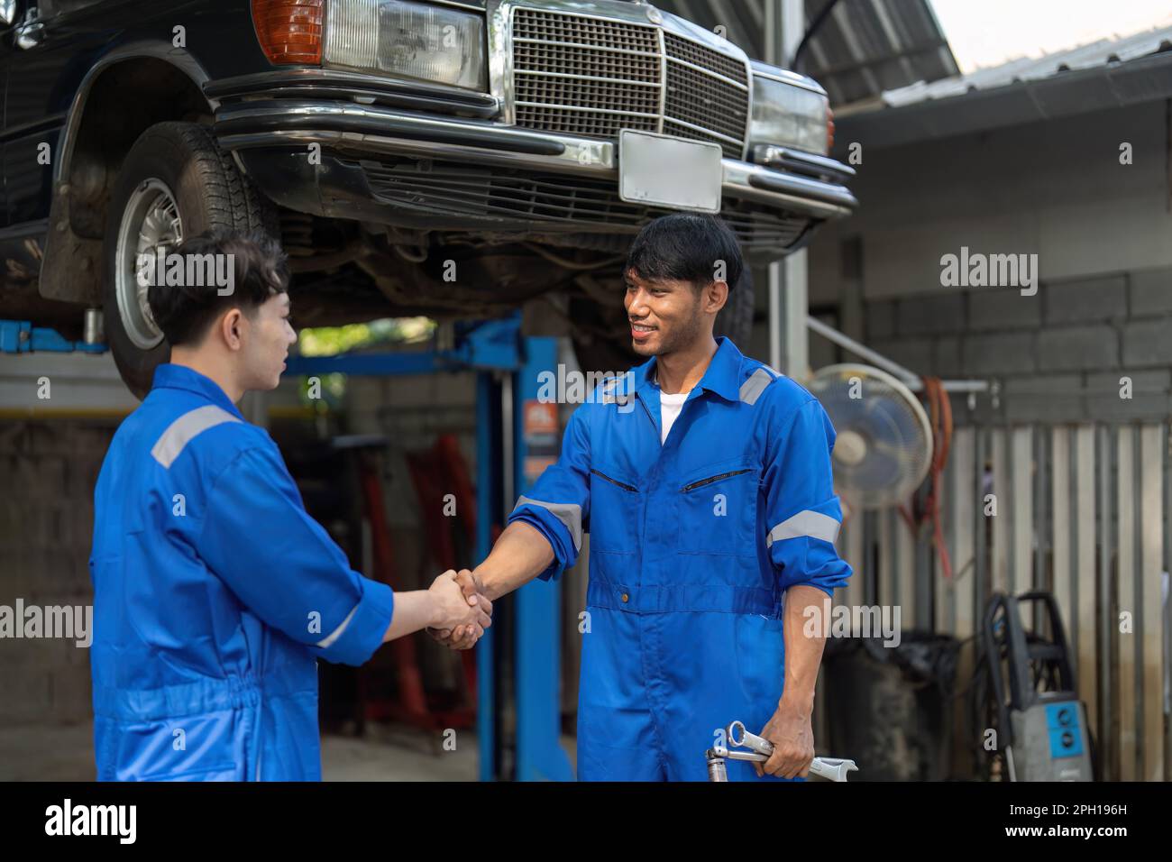 Two Asian automotive mechanic repairman handshake in garage. Vehicle ...