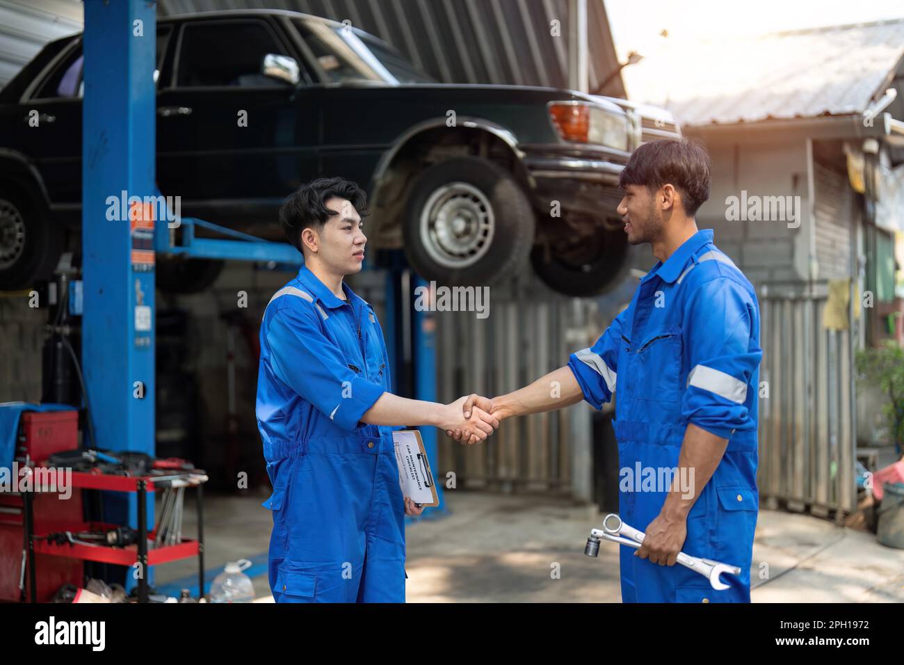 Two Asian automotive mechanic repairman handshake in garage. Vehicle ...