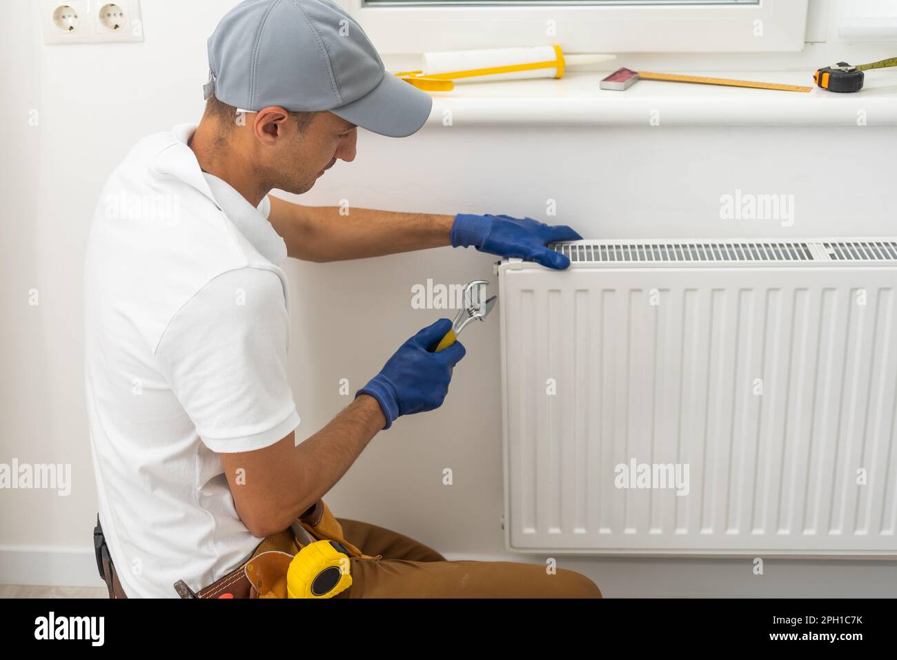 A male plumber installs a radiator in the heating system of an ...