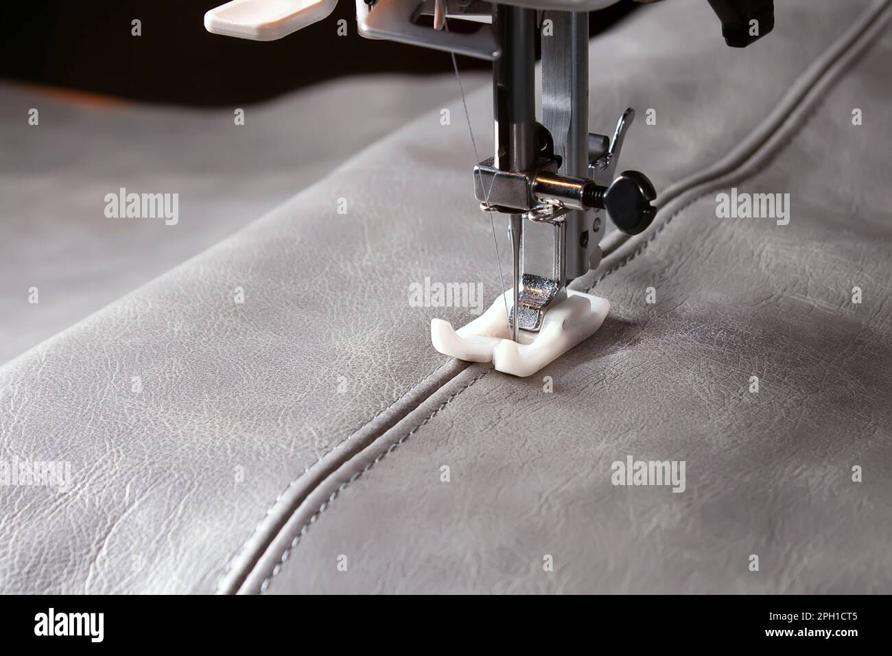 sewing machine with special presser foot makes a seam on grey leather ...