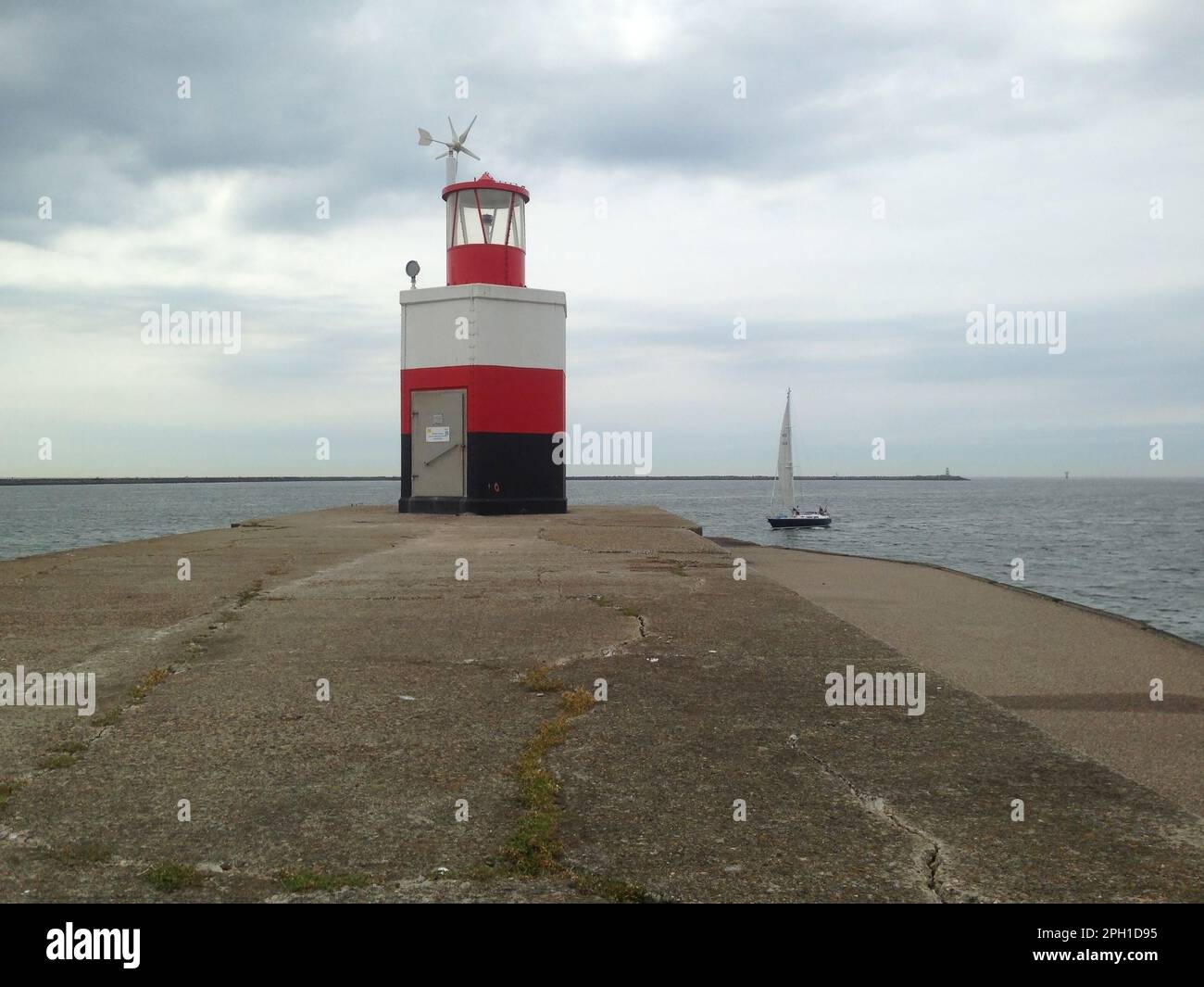 A small lighthouse at the end of a long concrete pier, its bright light ...