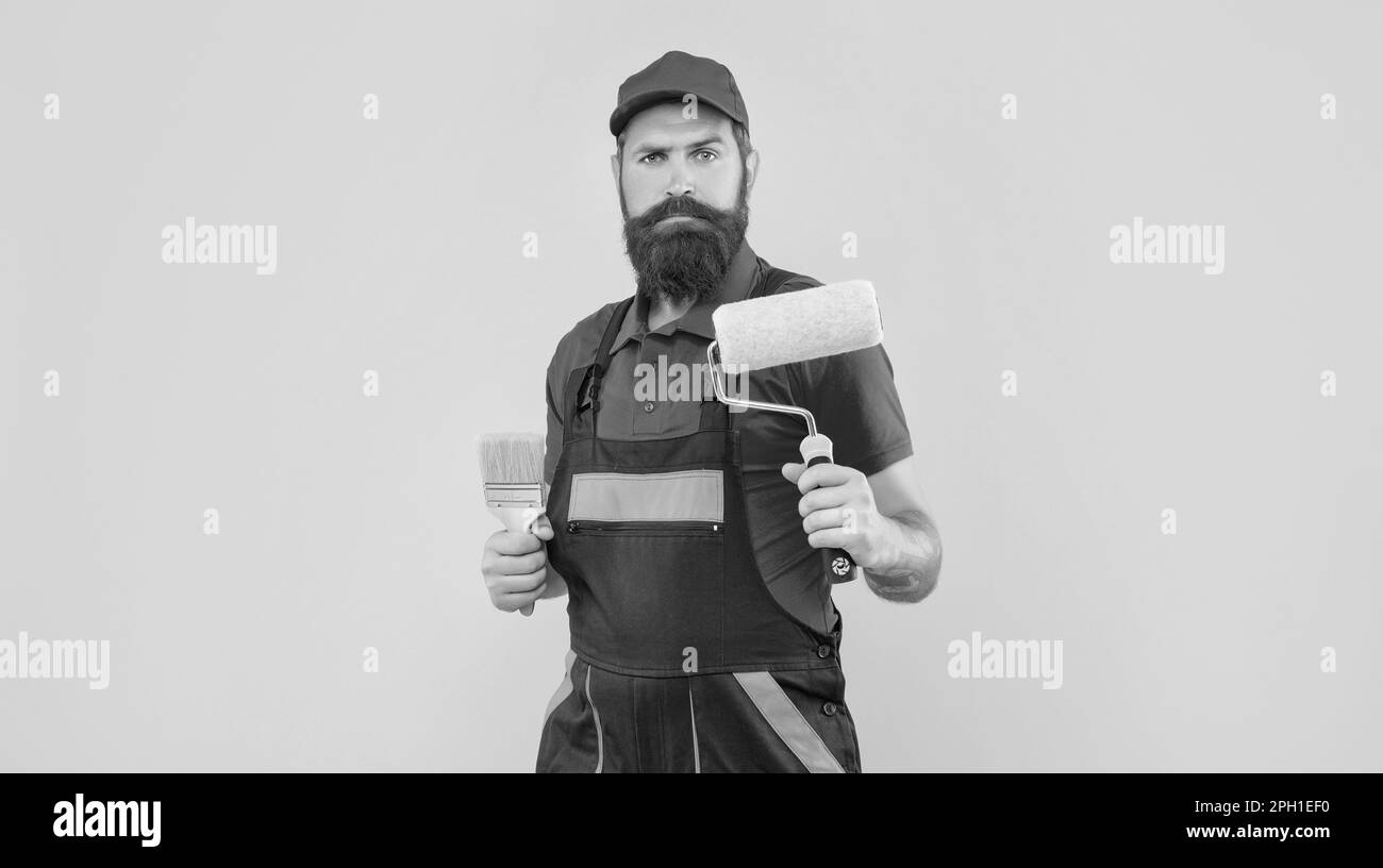 bearded man painter in work clothes hold paint roller and brush on ...