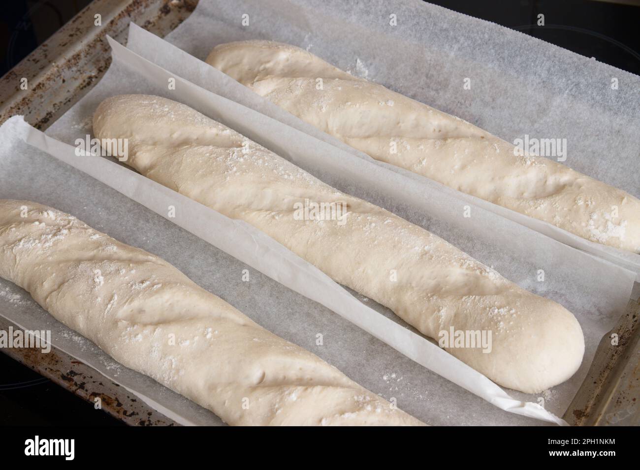 A baking tray with three loaves of raw bread with flour on top which ...