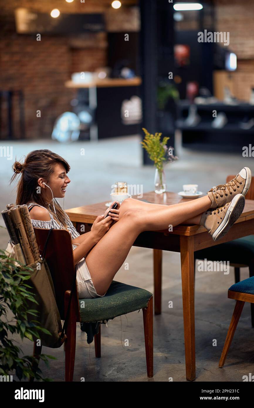 Beautiful young hipster girl with earphones, sitting alone at table ...