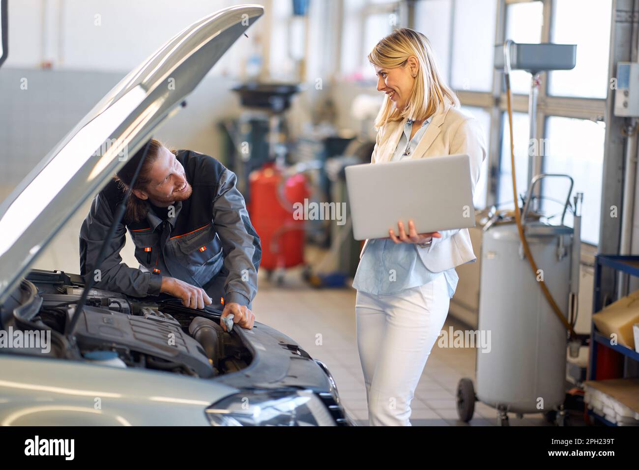 Happy worker in car workshop with young woman Stock Photo - Alamy