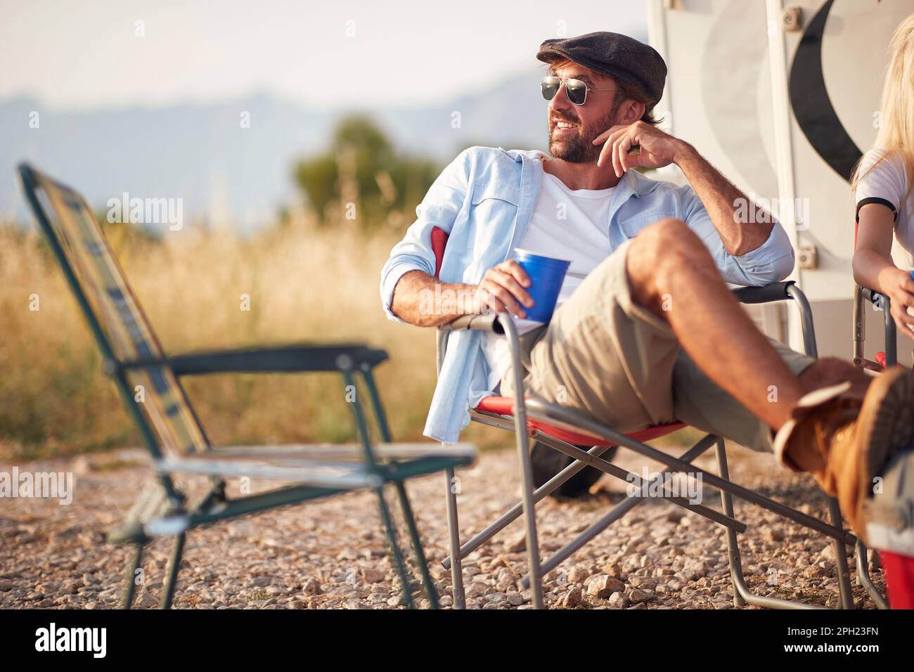 Handsome man with sunglasses and drink sitting in camper chair in front ...