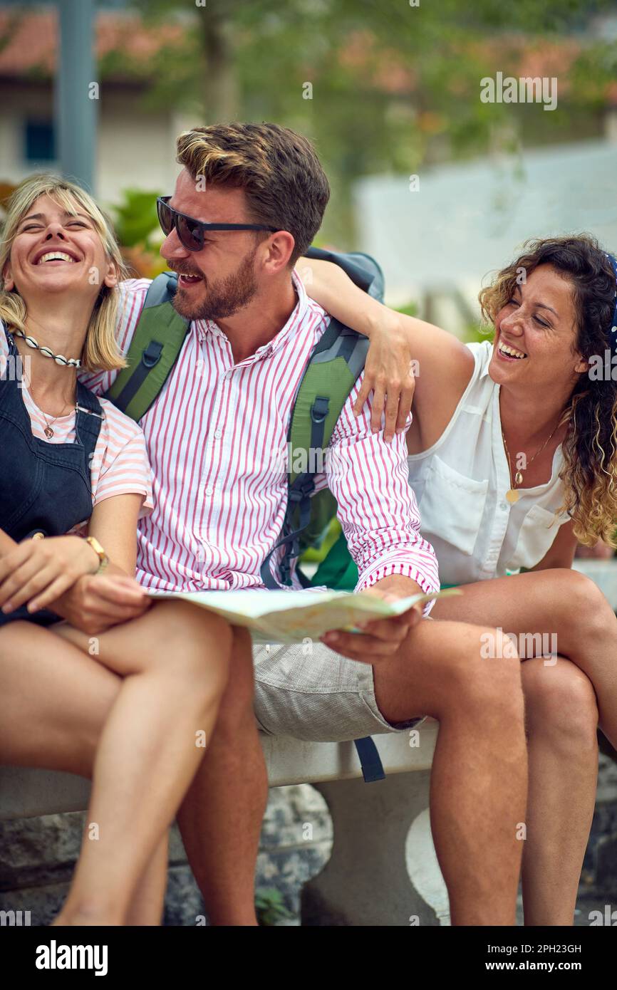 Young friends on bench holding map and laughing, tourists having fun ...