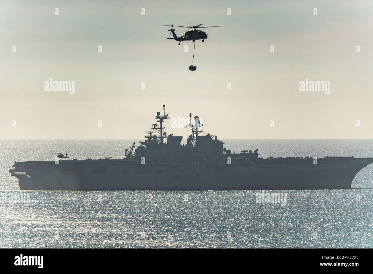 US Navy MH60S flys between a supply ship and the shoreline by Camp ...