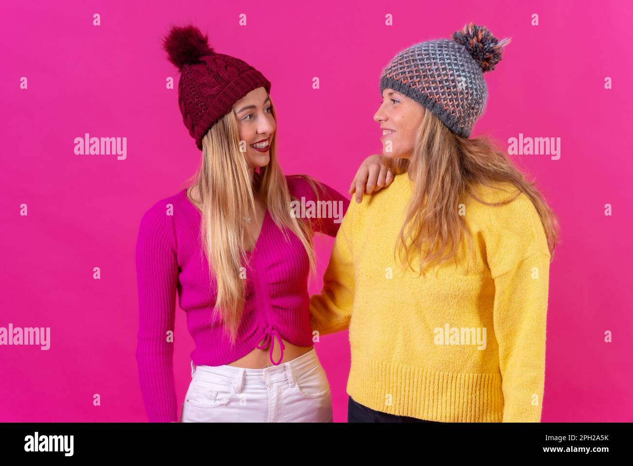 Two Females With Hats And Colorful Blouses Hugging Each Other Isolated On Vibrant Pink