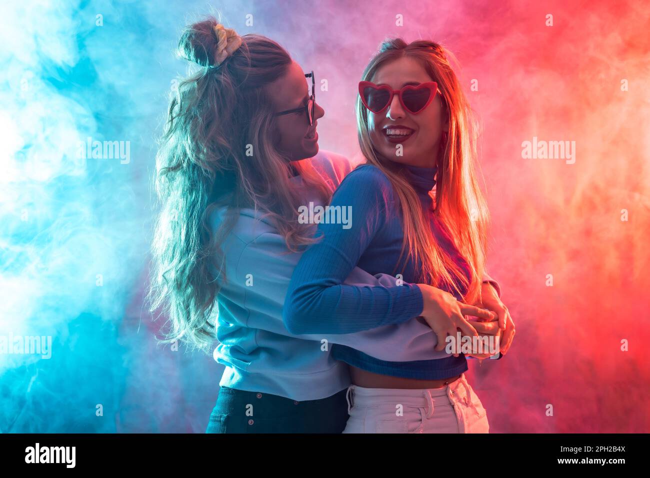 Two females embracing in a warm hug illuminated by bright neon lights ...