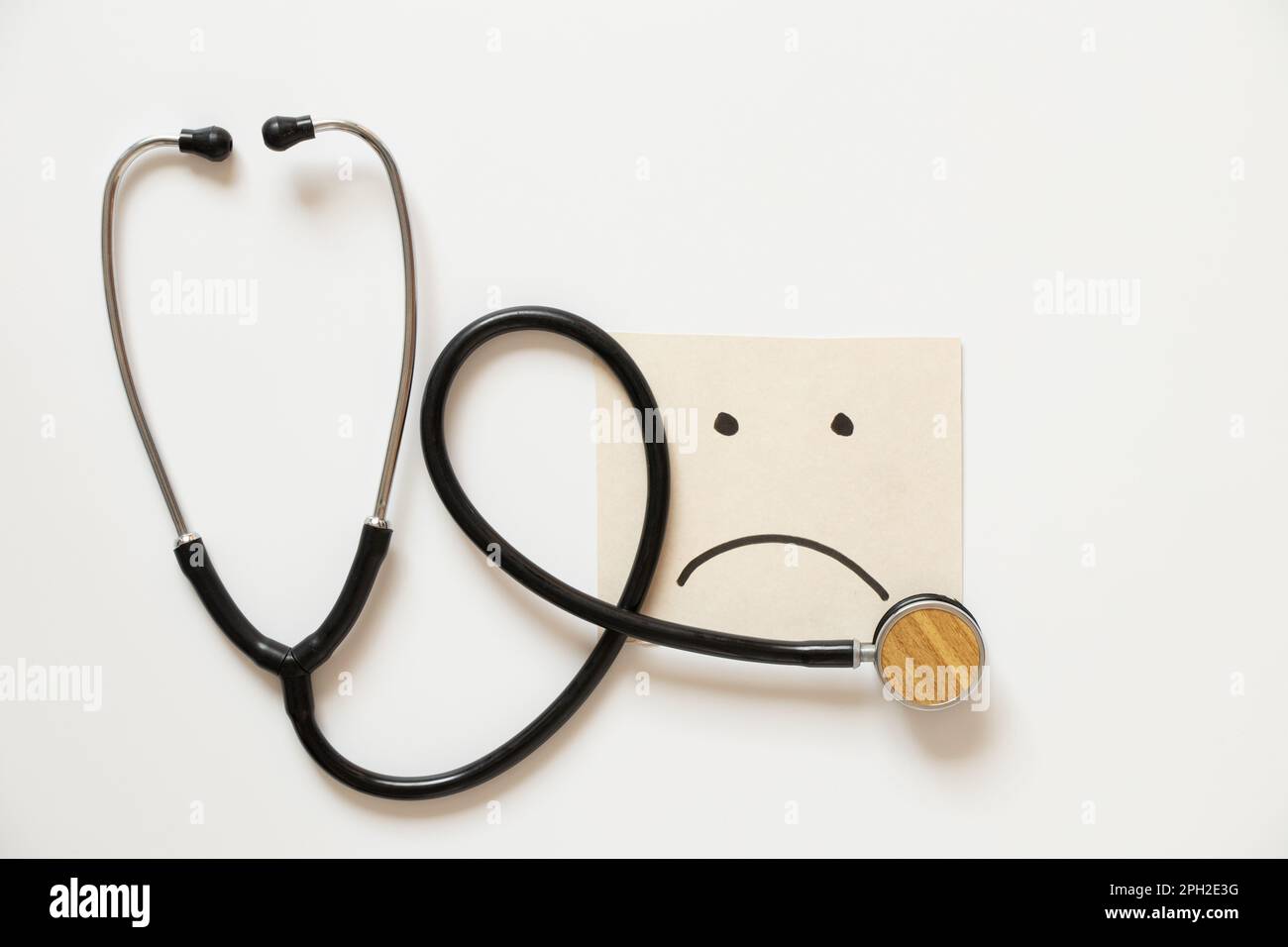 A stethoscope and a sad emoticon are drawn on a paper card on a white ...