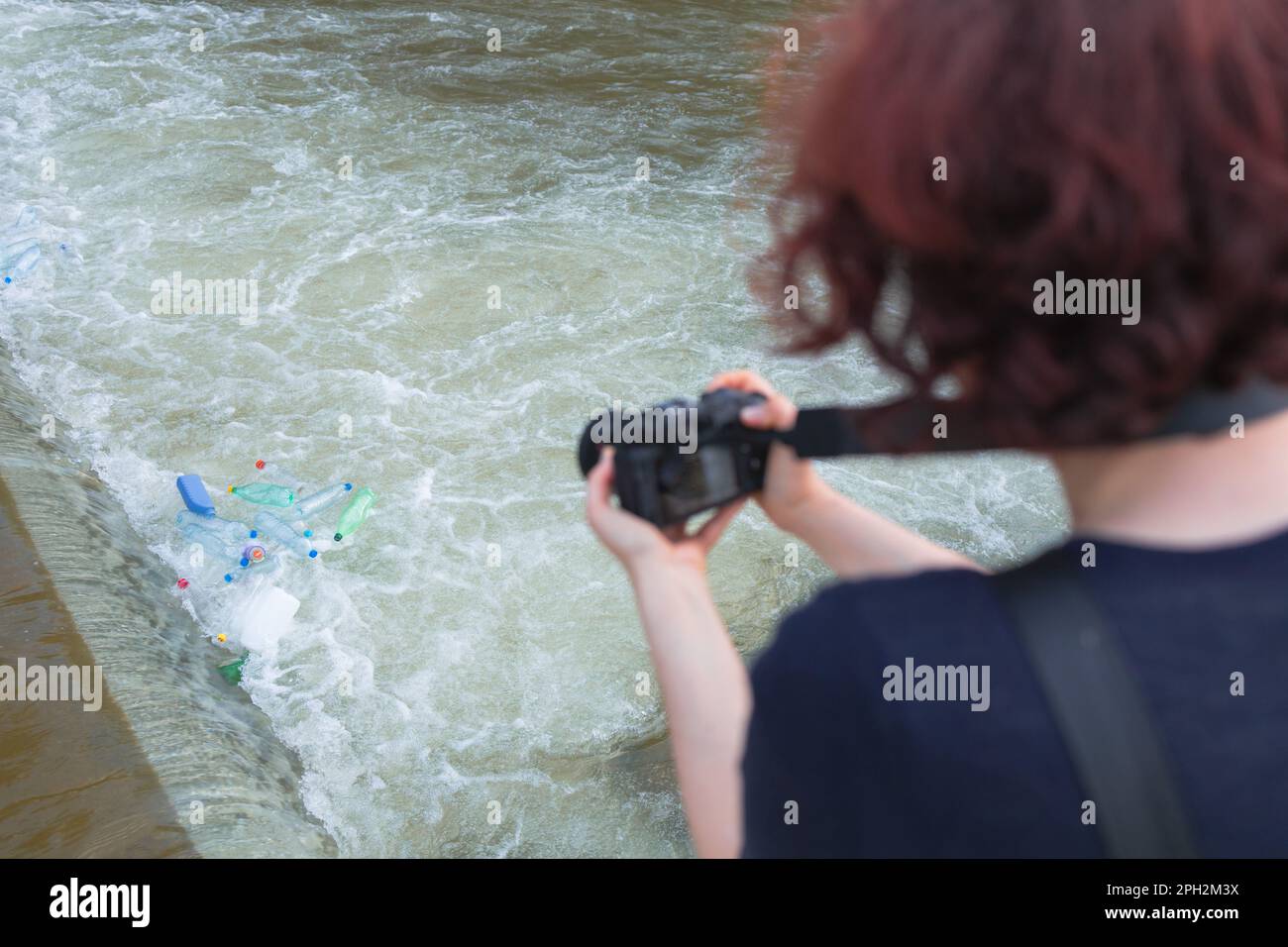 Female photographer photographing garbage in the river, plastic bottles ...