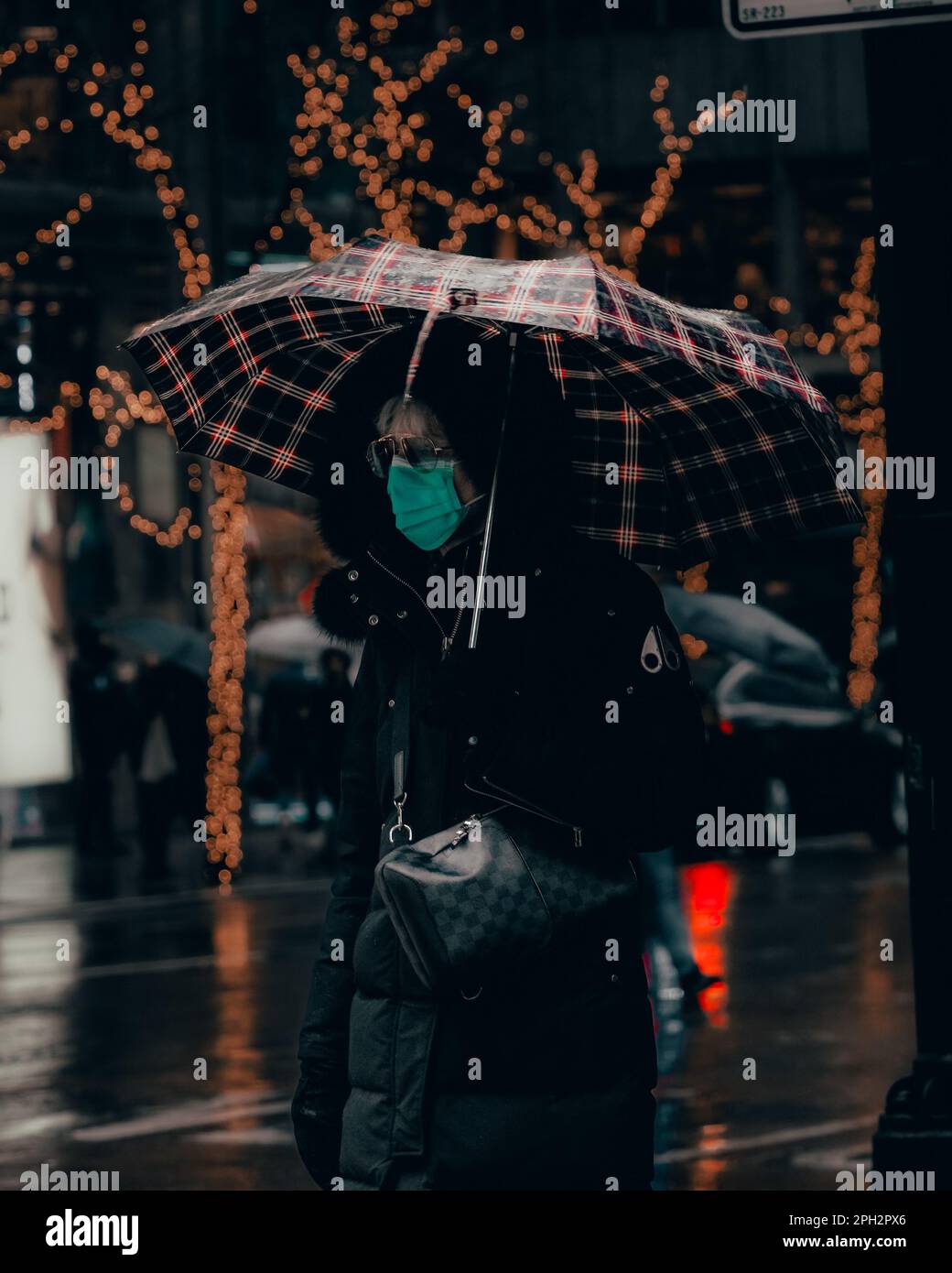 Women with umbrella and mask with lights in the background on a street ...