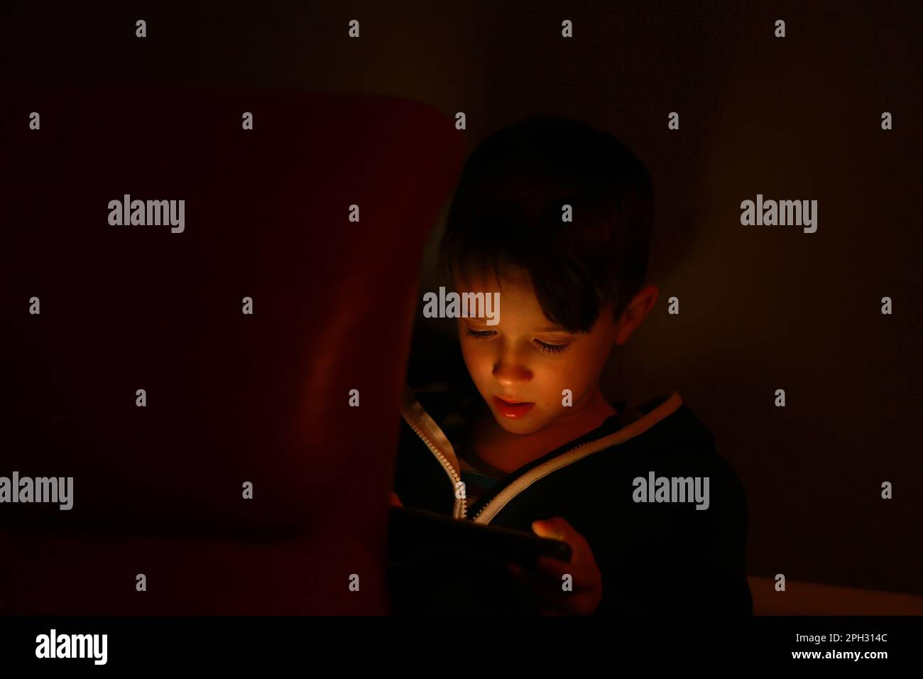 Little boy playing with tablet or cellphone in the dark. Kids face ...