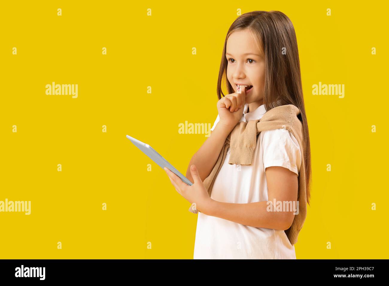 Little girl with tablet computer biting nails on yellow background ...