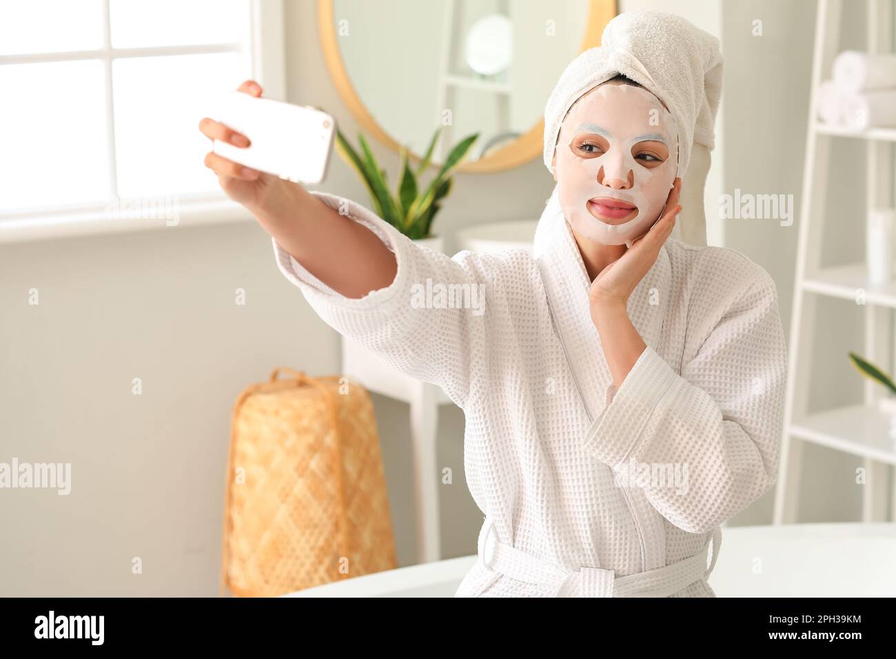 Young woman with sheet mask taking selfie in bathroom Stock Photo - Alamy