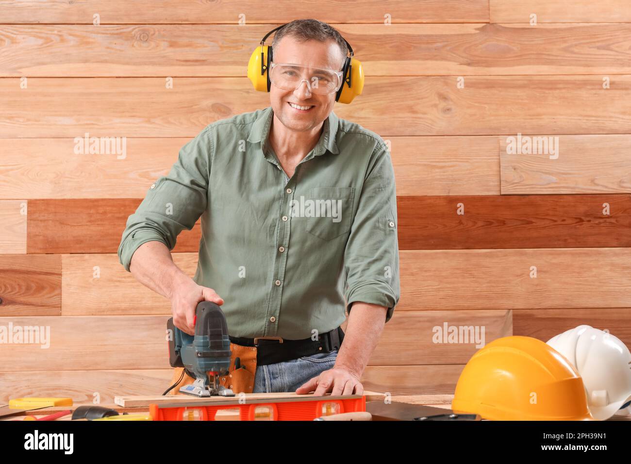 Mature carpenter sawing plank at table near wooden wall Stock Photo - Alamy